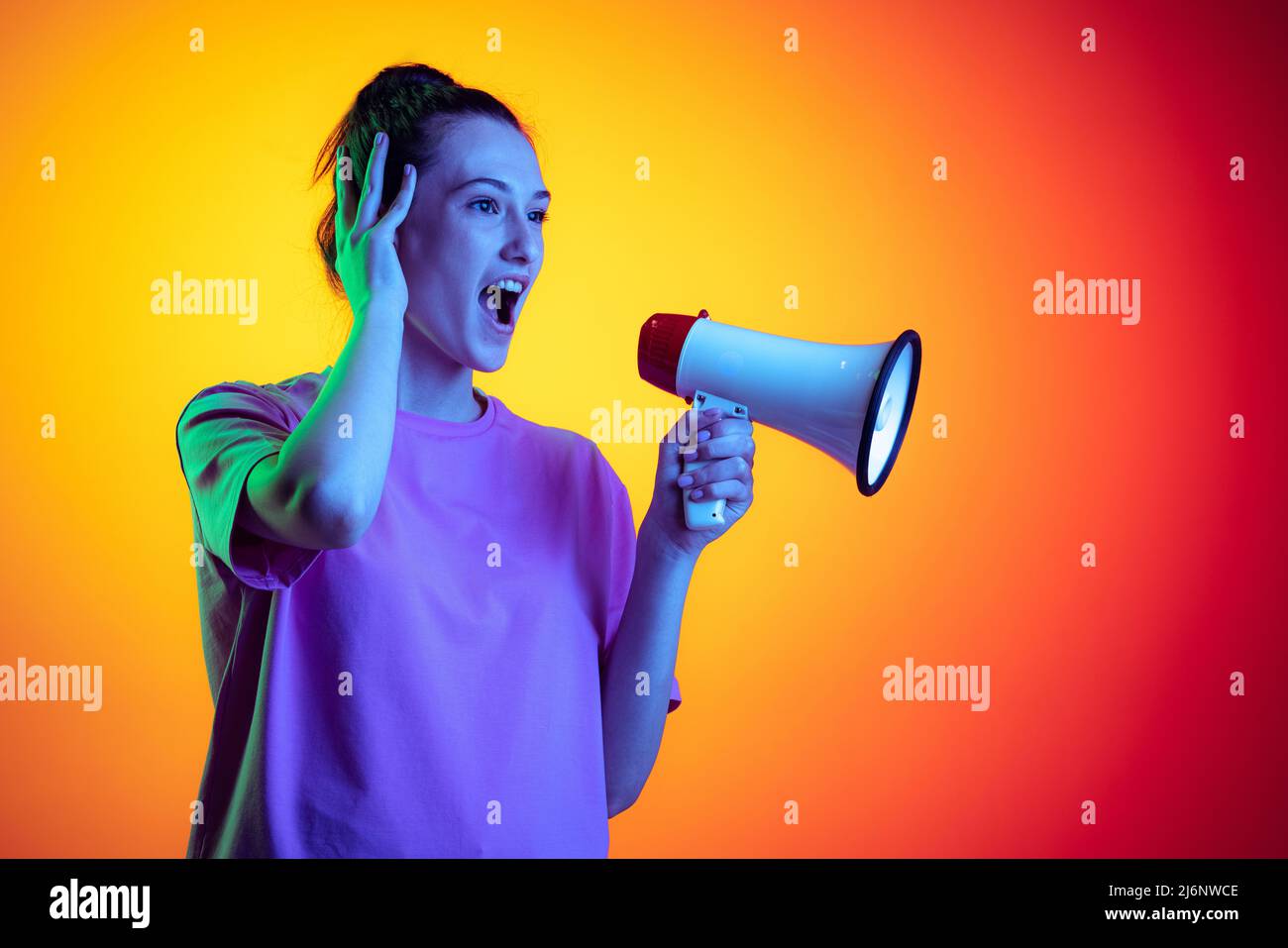 Beautiful excited girl shouting at megaphone isolated on yellow-red ...