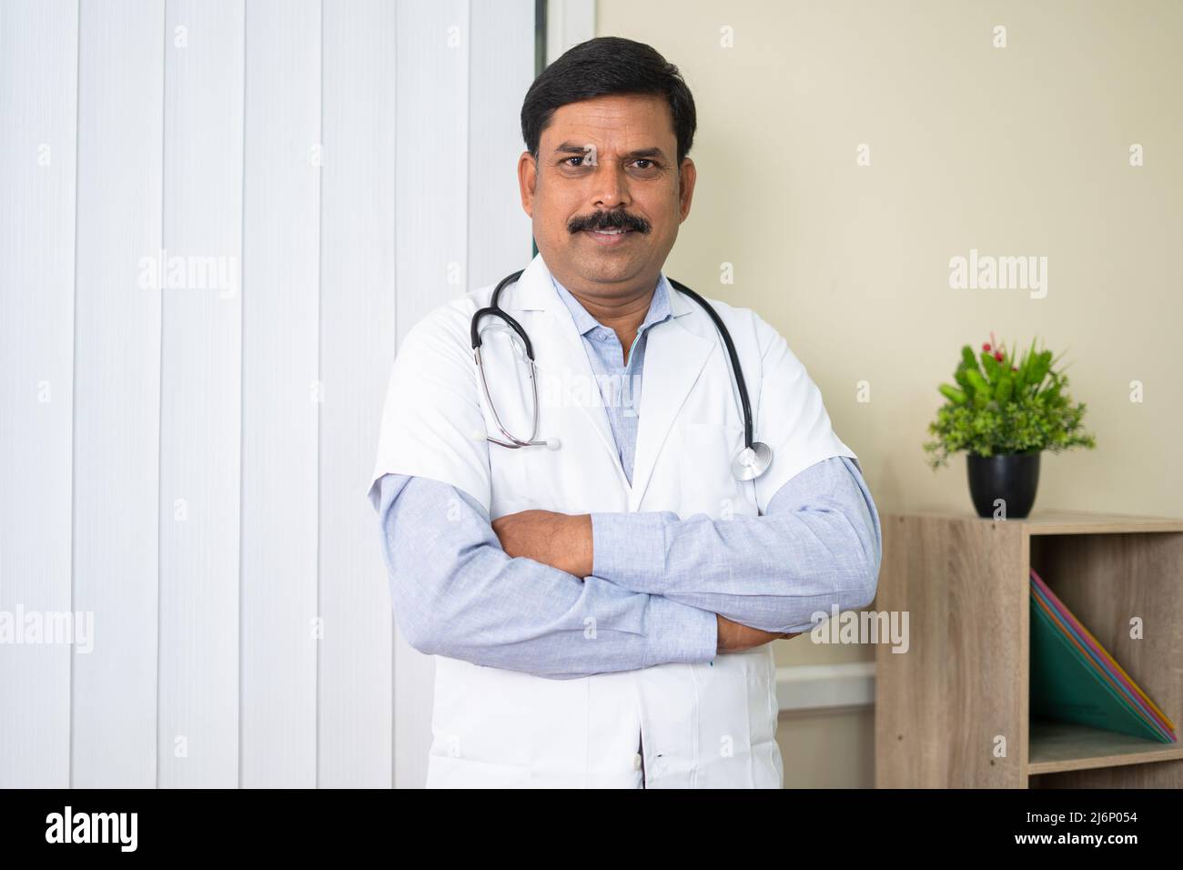 Confident doctor standing with arms crossed by looking at camera at ...