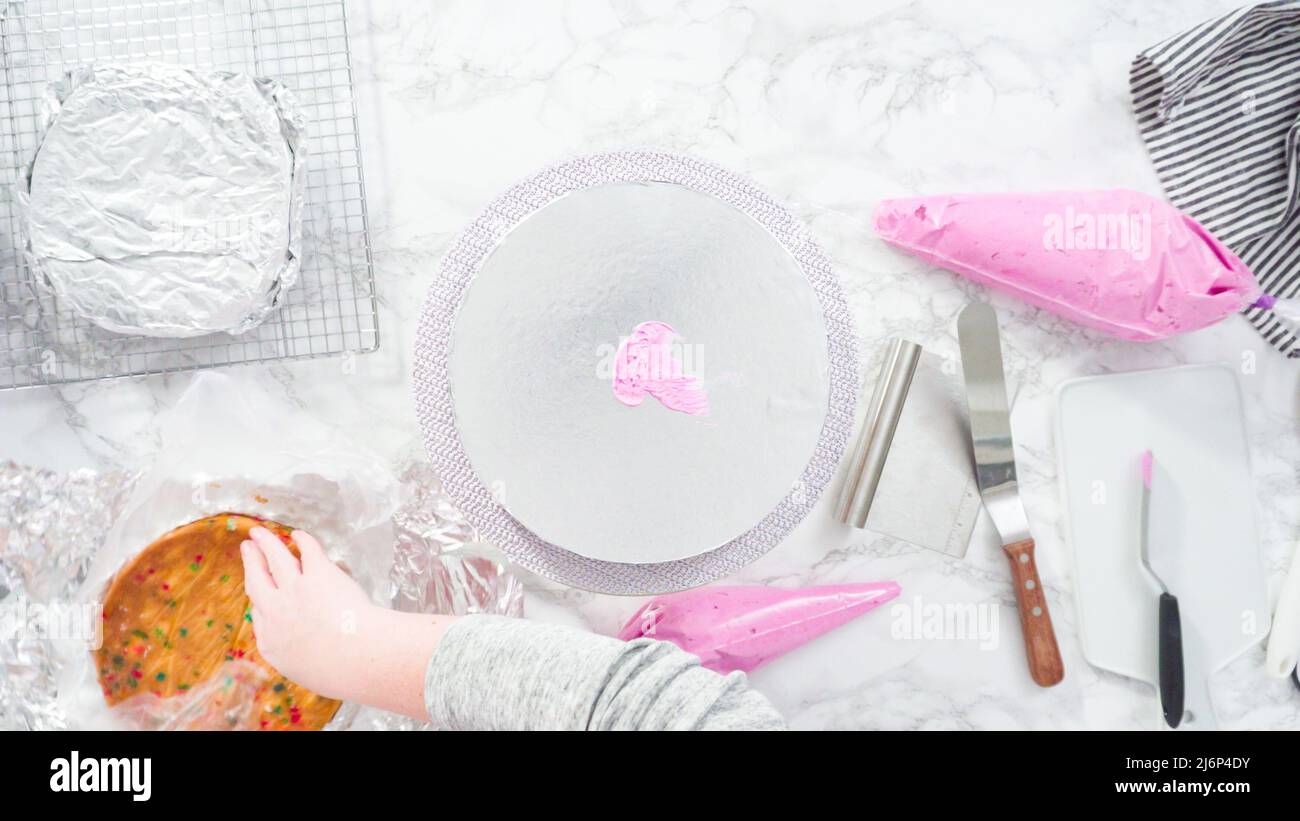 Flat lay. Step by step. Frosting round funfetti cake layers with pink ...