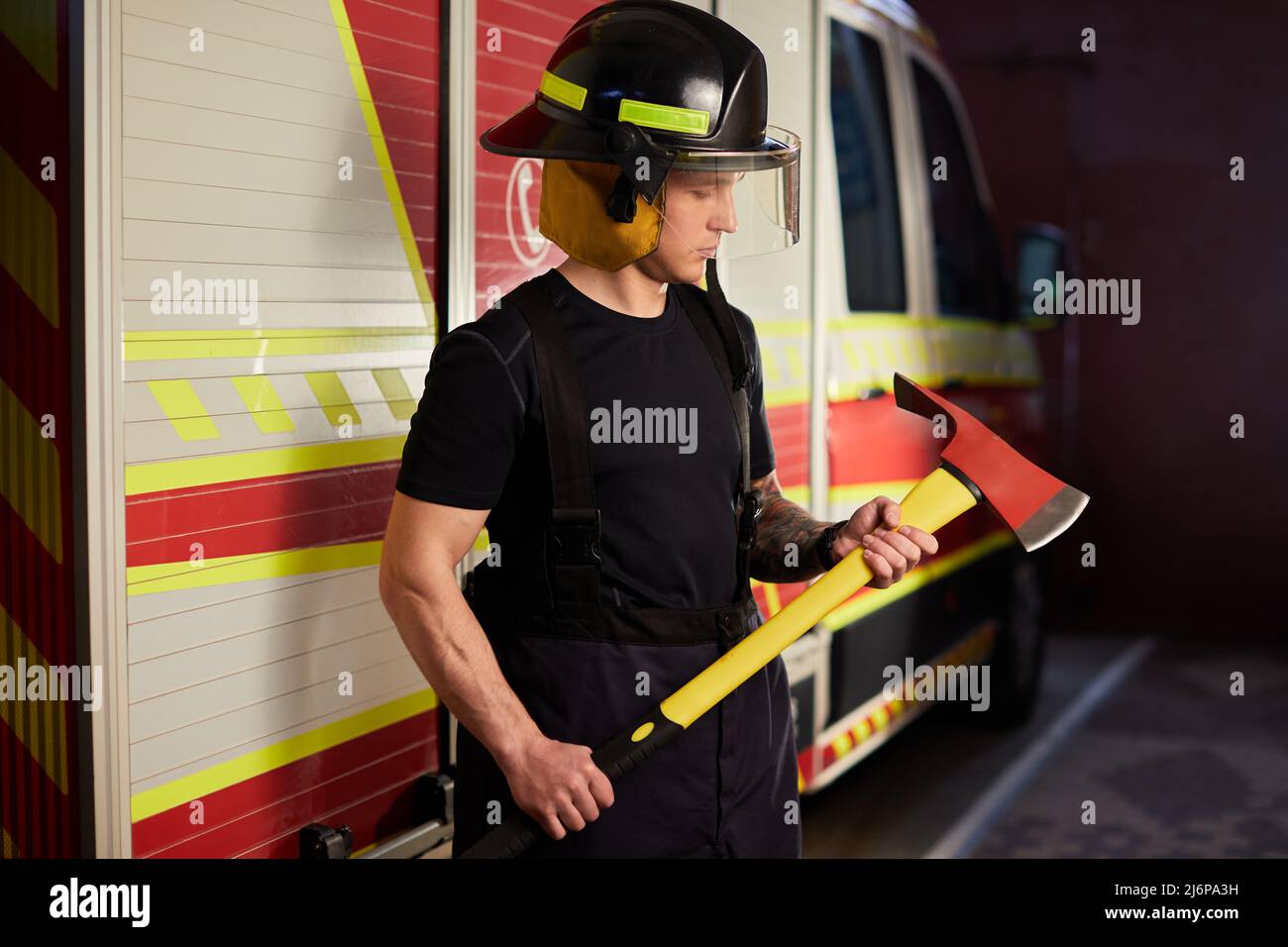 Photo of fireman wearing helmet with ax against fire engine Stock Photo ...
