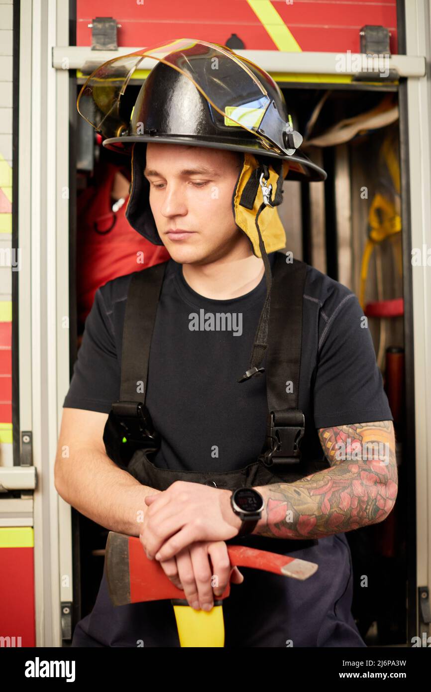 Photo of fireman wearing helmet with ax against fire engine Stock Photo ...
