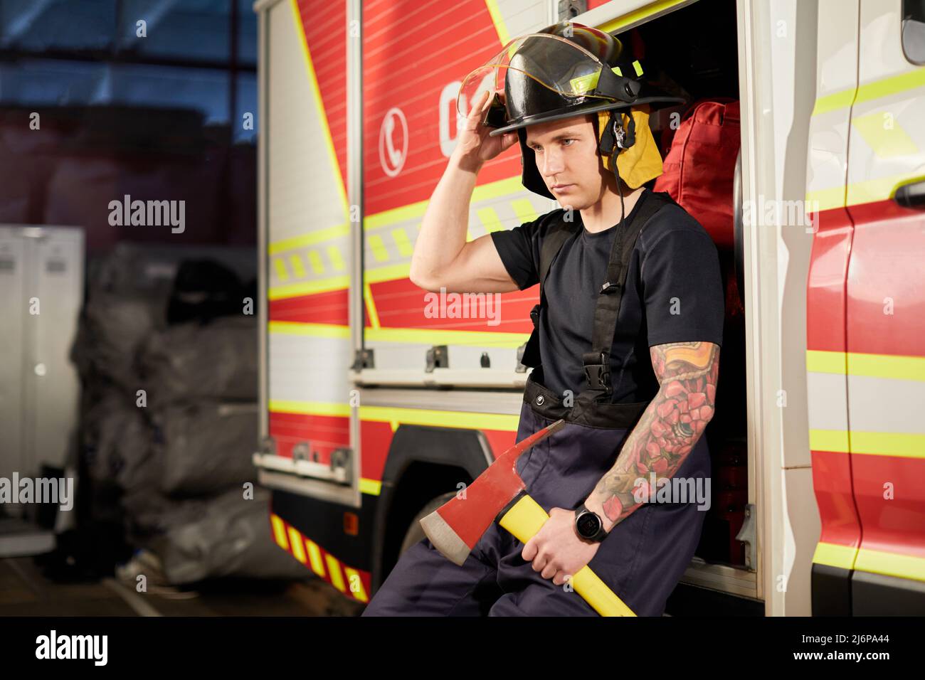 Photo of fireman wearing helmet with ax against fire engine Stock Photo ...