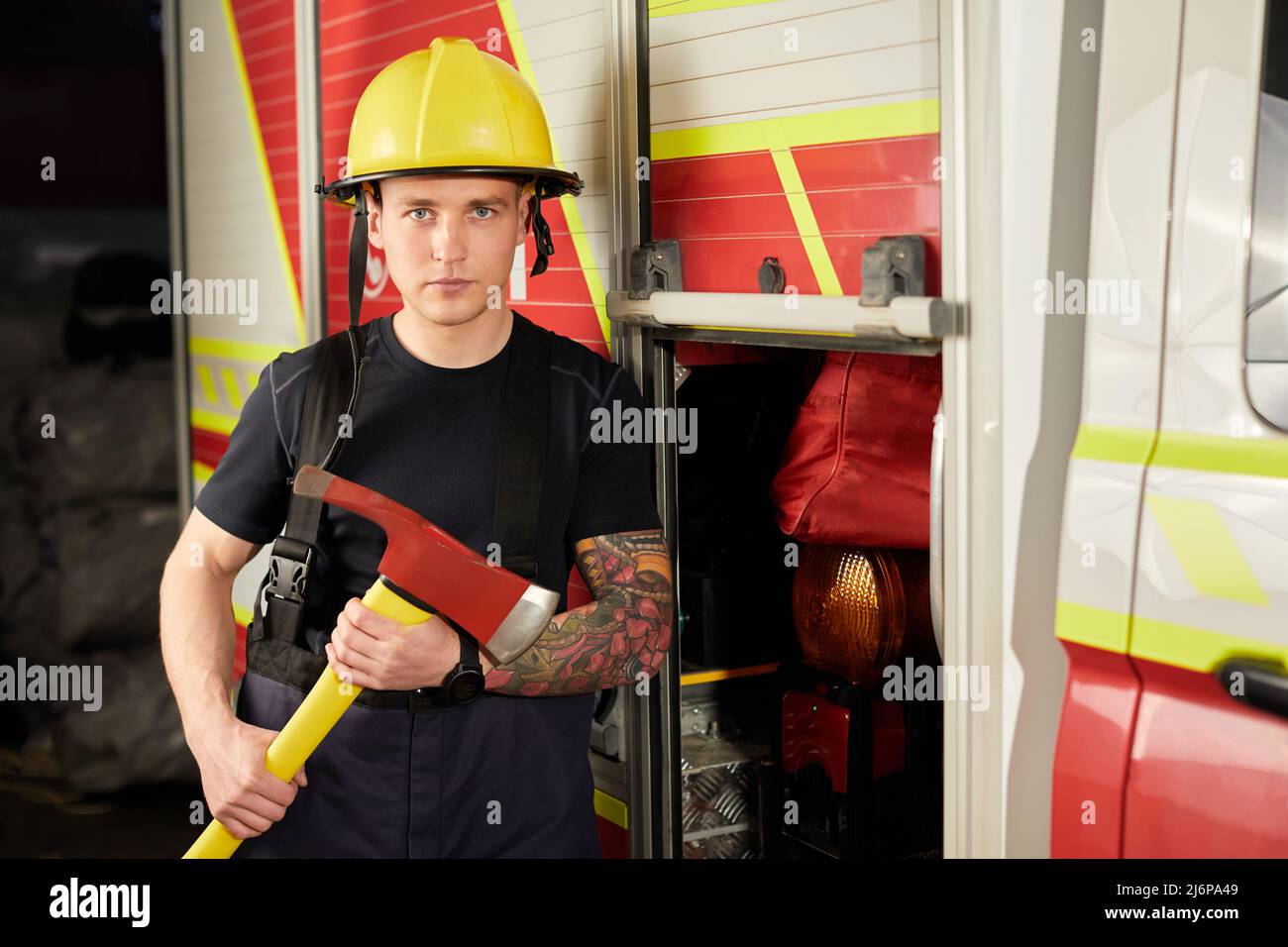 Photo of fireman wearing helmet with ax against fire engine Stock Photo ...