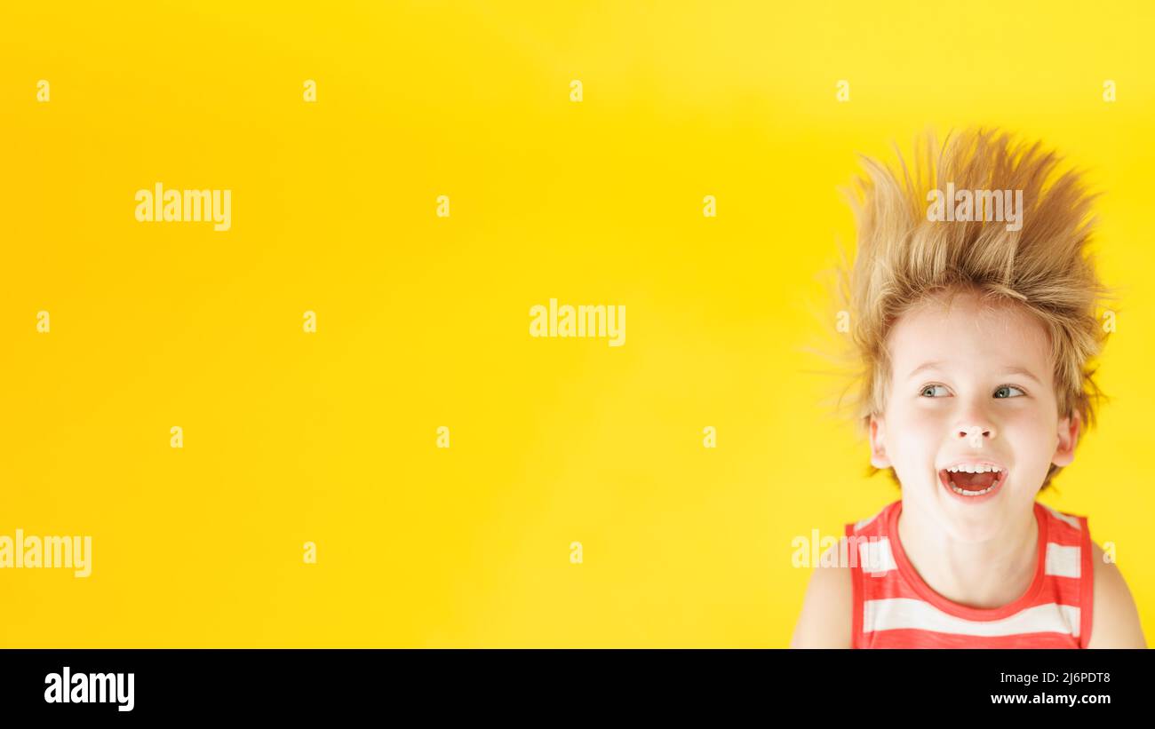 Happy child shouting against yellow paper background. Funny kid hanging ...