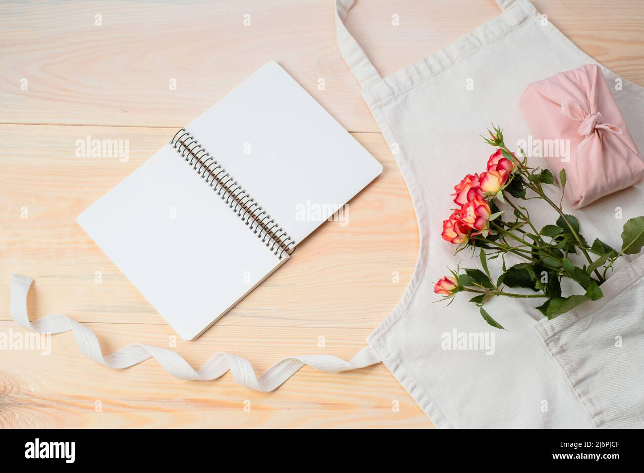 Blank diary with a pink rose, gift wrapped in cloth, apron on a wooden ...
