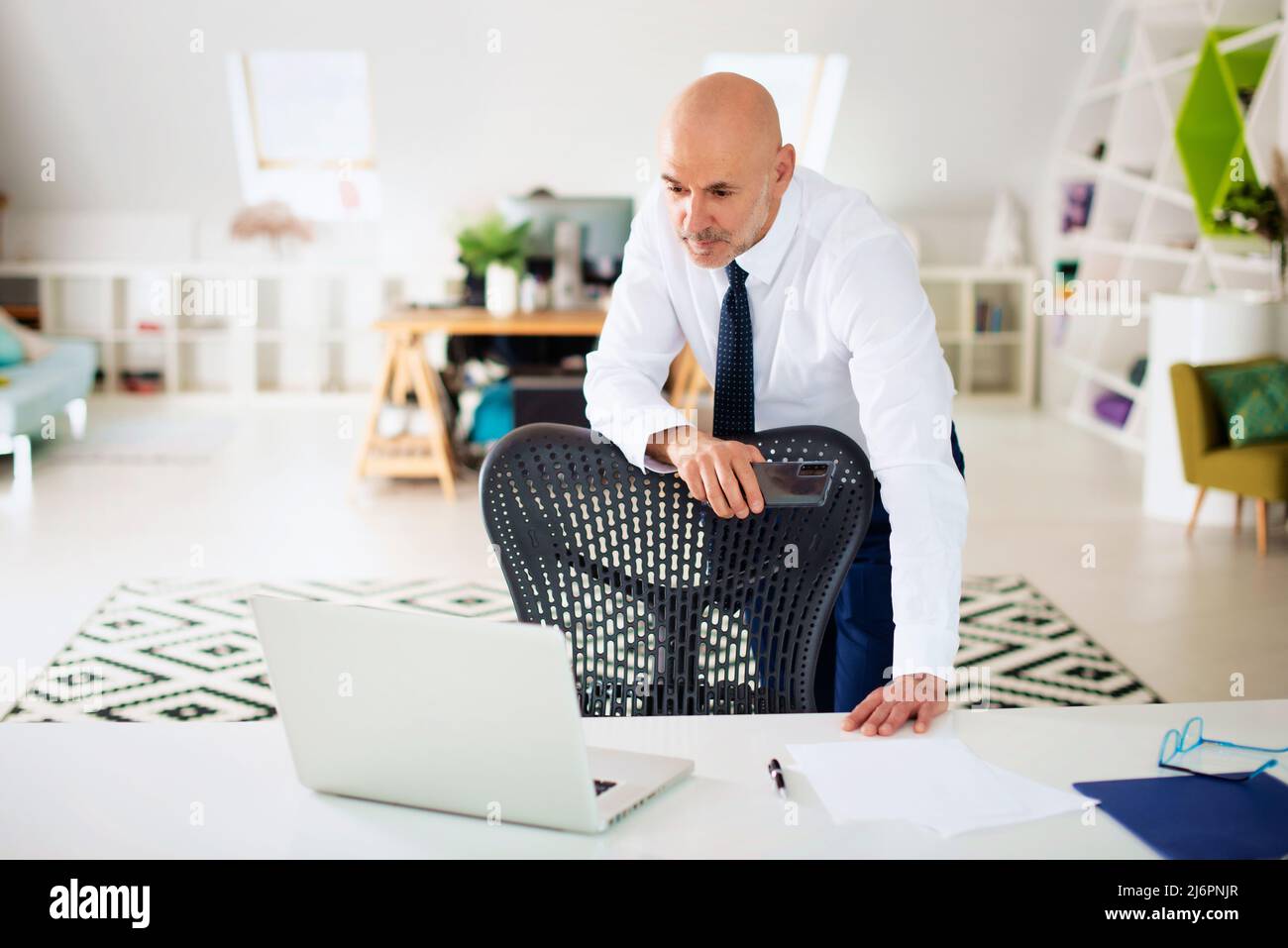 Thinking businessman standing at desk at the office and using laptop ...