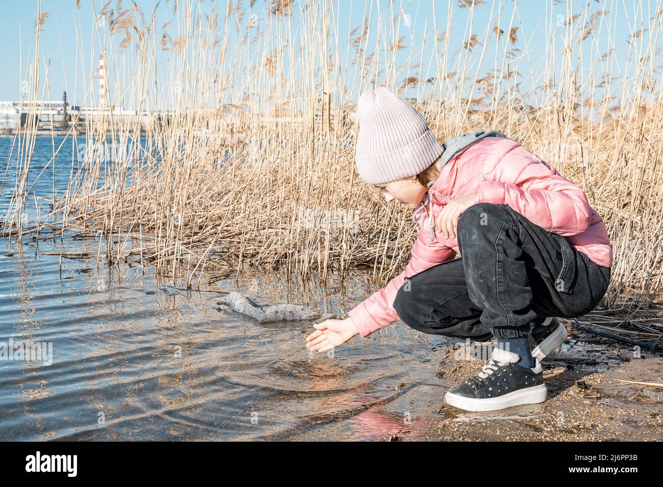 Charming girl in warm clothes plays on the shore of the lake. Sunny ...