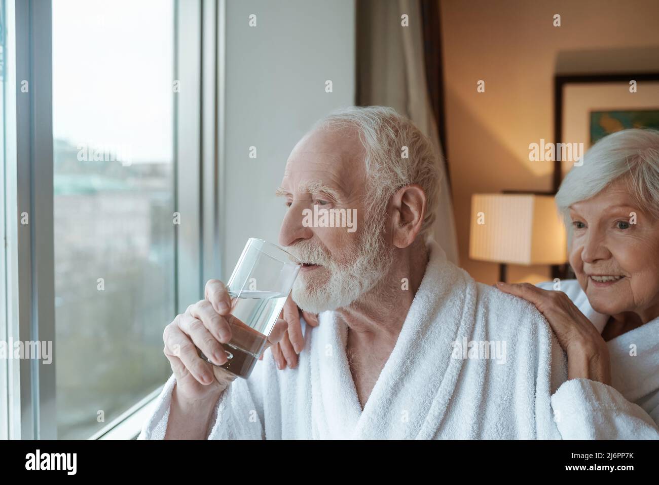 A happy elderly couple standing near the window in the hotel Stock ...