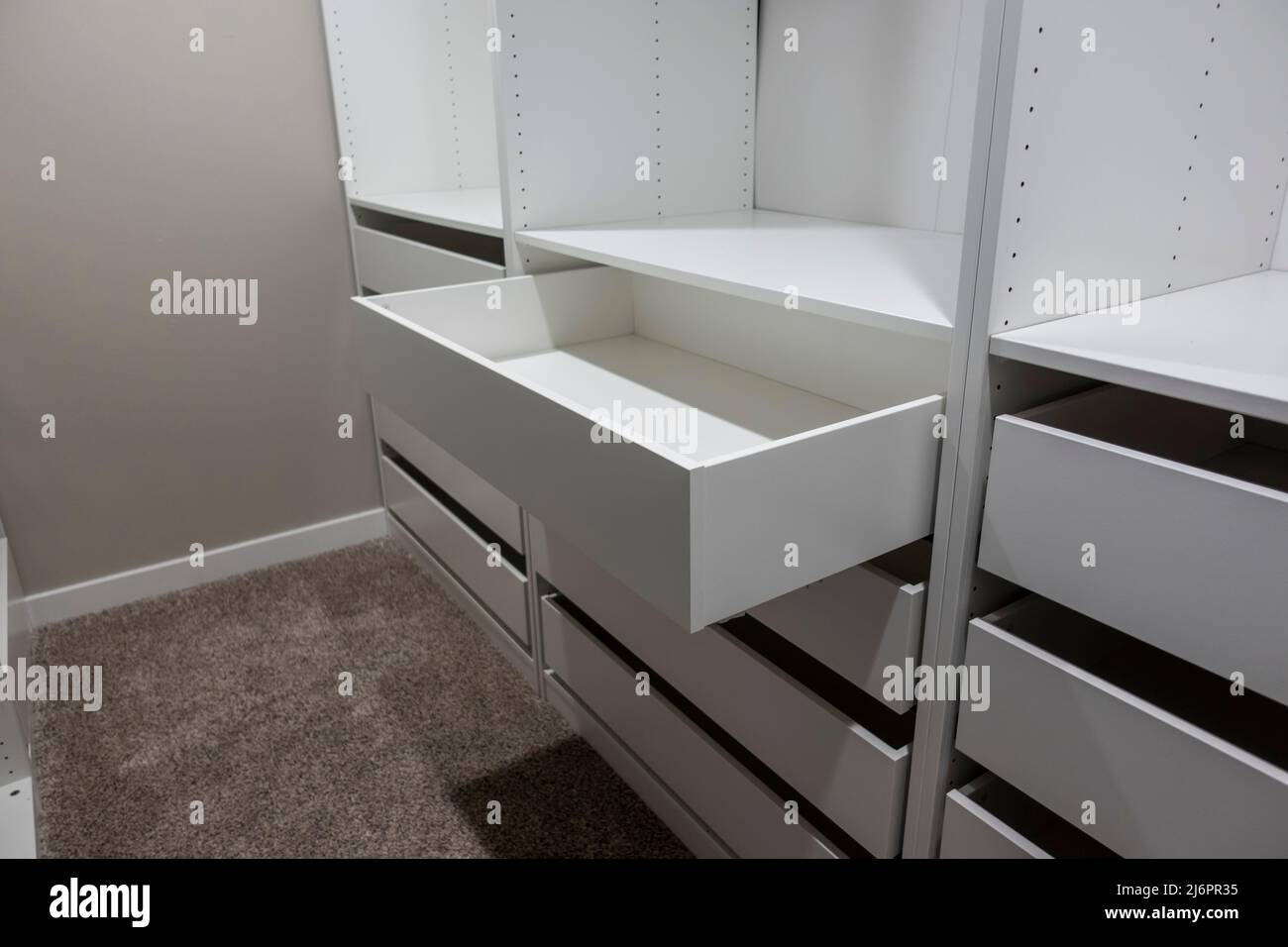 View of tall, white cabinets and drawers inside a narrow walk in closet ...