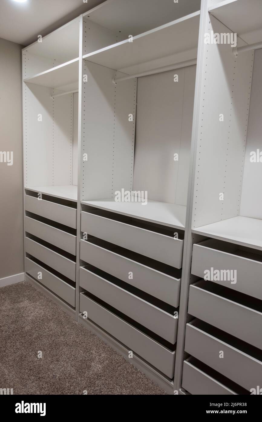 View of tall, white cabinets and drawers inside a narrow walk in closet ...