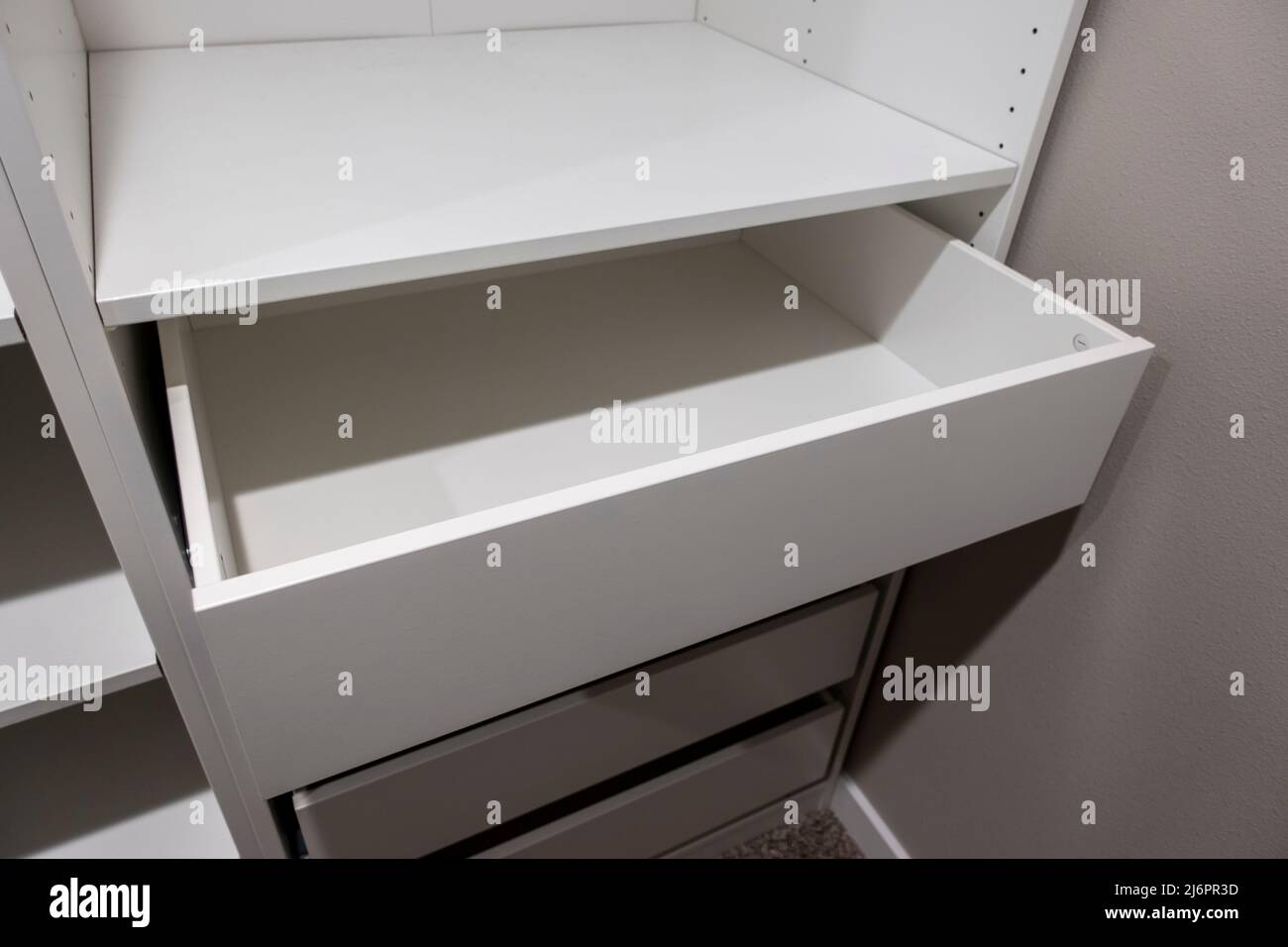 View of tall, white cabinets and drawers inside a narrow walk in closet ...