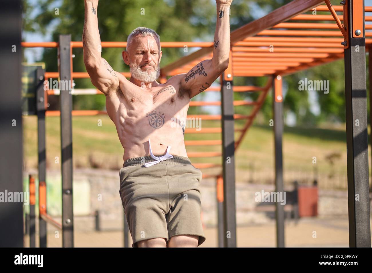 A gray-haired mature man having a workout on the open sports ground ...
