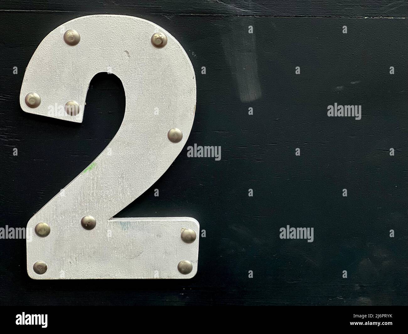 White wooden number two with nail heads on black background, copy space ...
