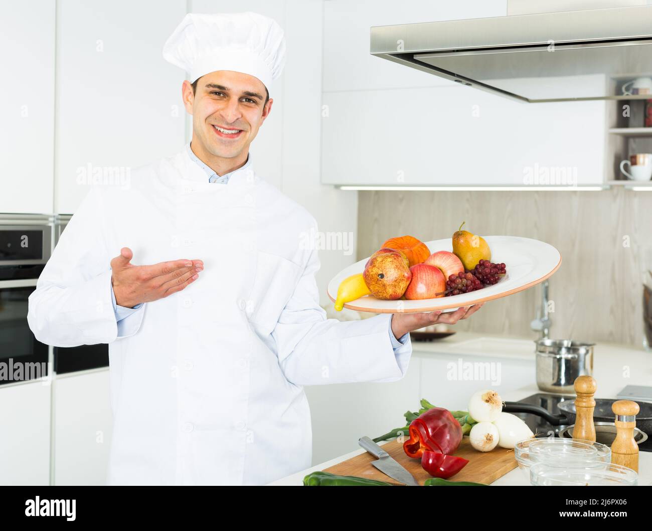 Smiling male kitchener in uniform is posing with plate of fruits in the ...