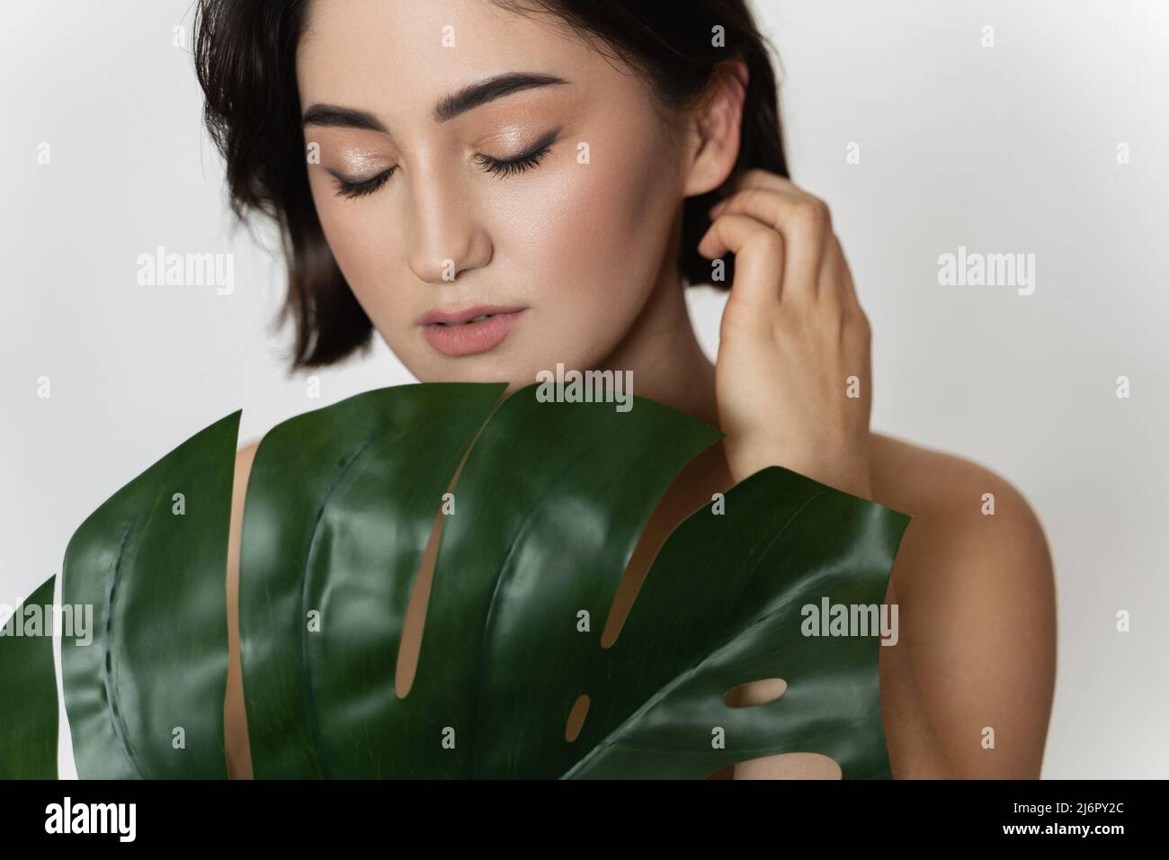 Beautiful woman with a smooth skin holding green tropical leaf on white ...
