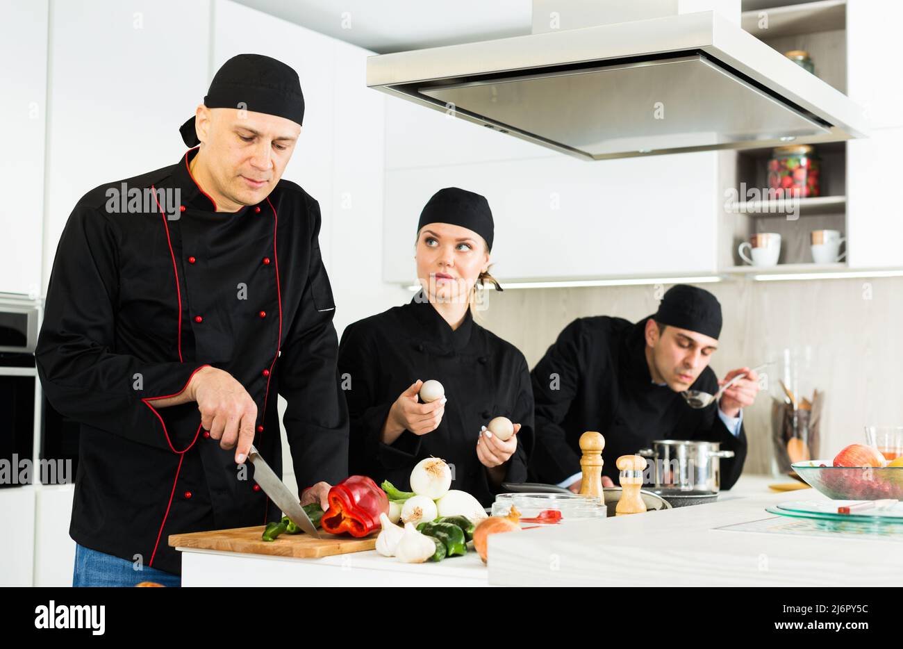Female and two male cooks are making salad on their work place in the ...