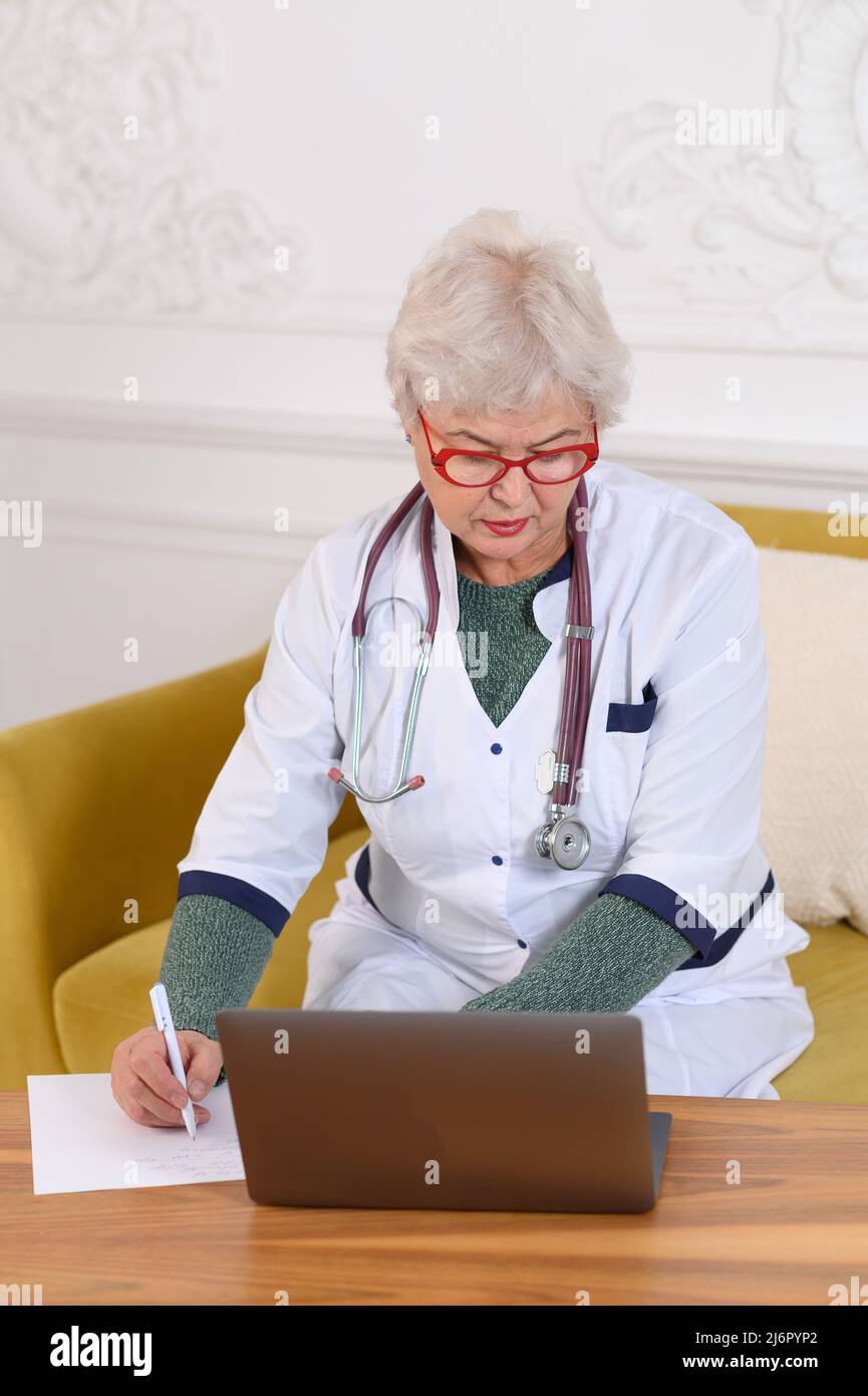 Middle age female doctor using laptop, writing notes with stethoscope ...