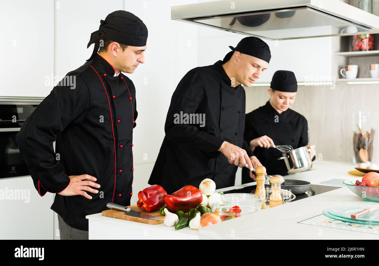 Female and two male cooks are making salad on their work place in the ...