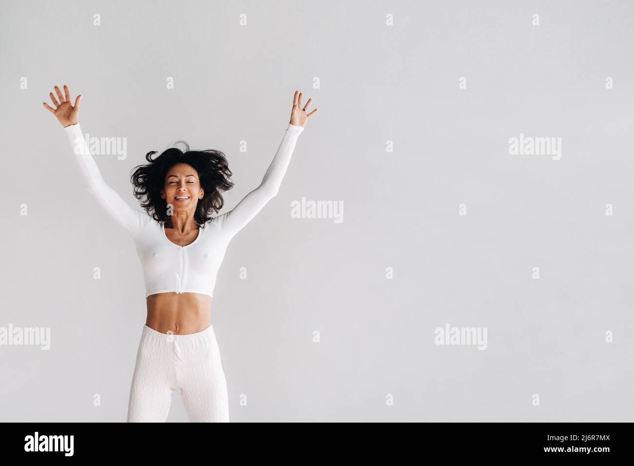 A happy woman in white sportswear bounces on a white background. The ...