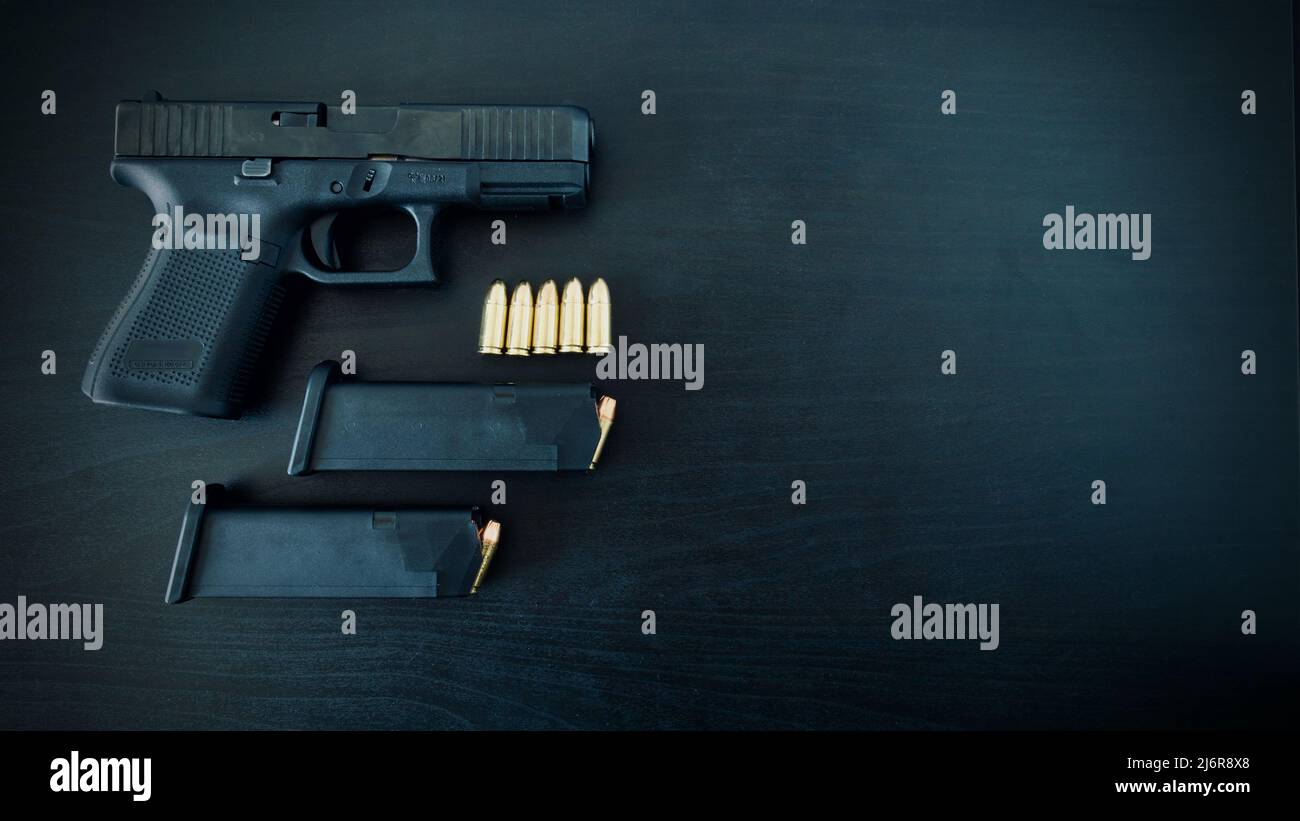 Handgun with two magazines and 9 mm ammo on black wooden table with ...