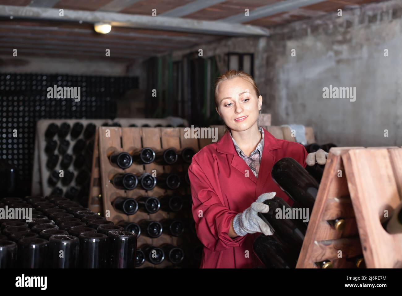 Woman in uniform working with bottle storage racks in winery cellar ...