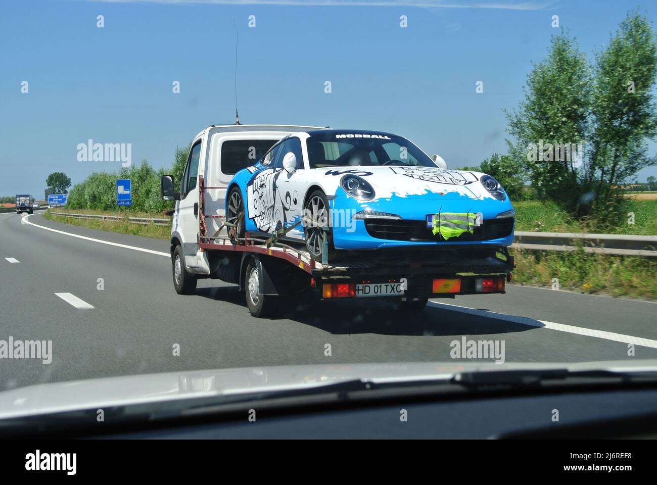 A Porsche racing car transported on the rear of a flatbed lorry on a ...