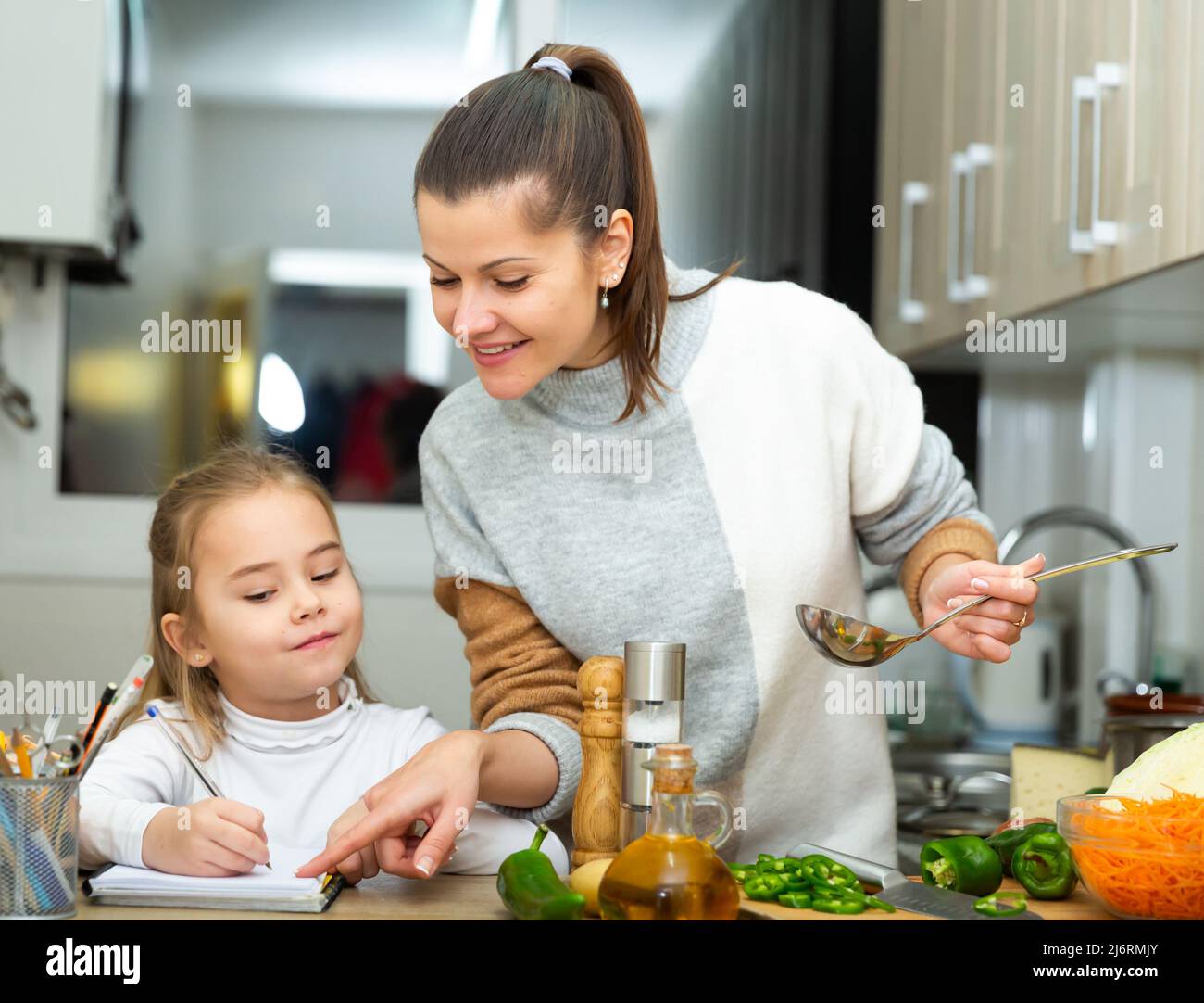 Girl writing school lesson during mother cooking at kitchen Stock Photo ...