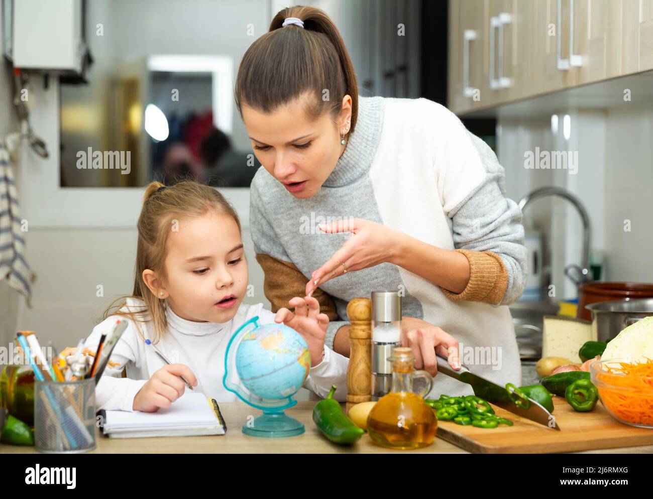 Mother cooking and little daughter doing school homework Stock Photo ...