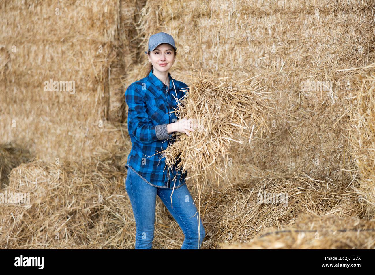 Young female farmer standing in hayloft with hay in hands Stock Photo ...