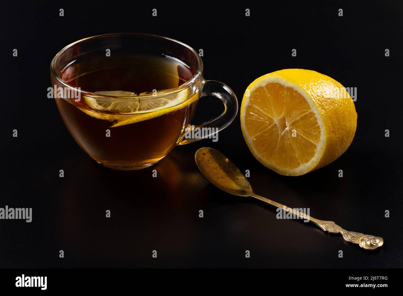 Glass cup of tea with pieces of lemon, a spoon on the black background ...