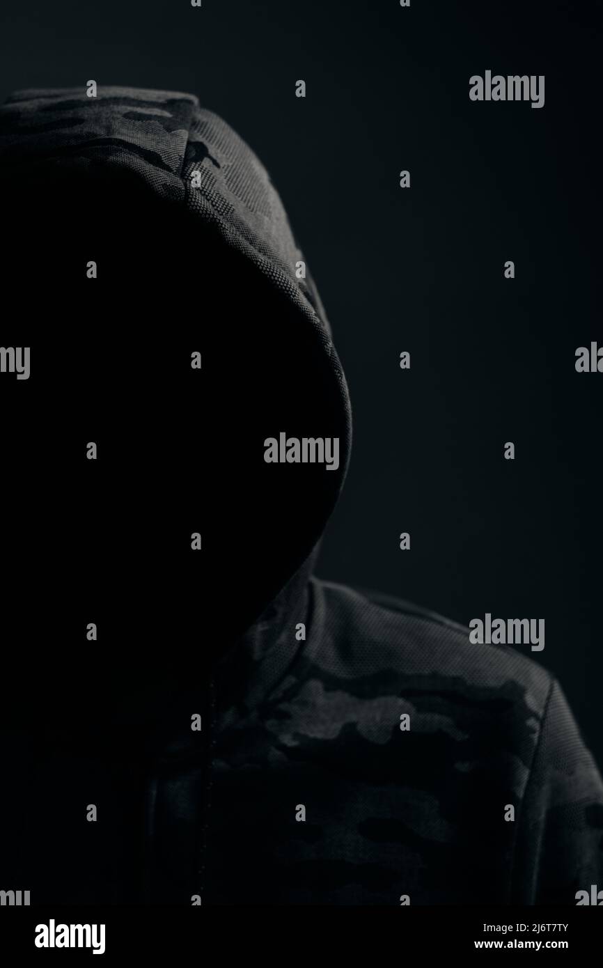 Man in dark camouflage hoodie with covered face dark background, hacker ...