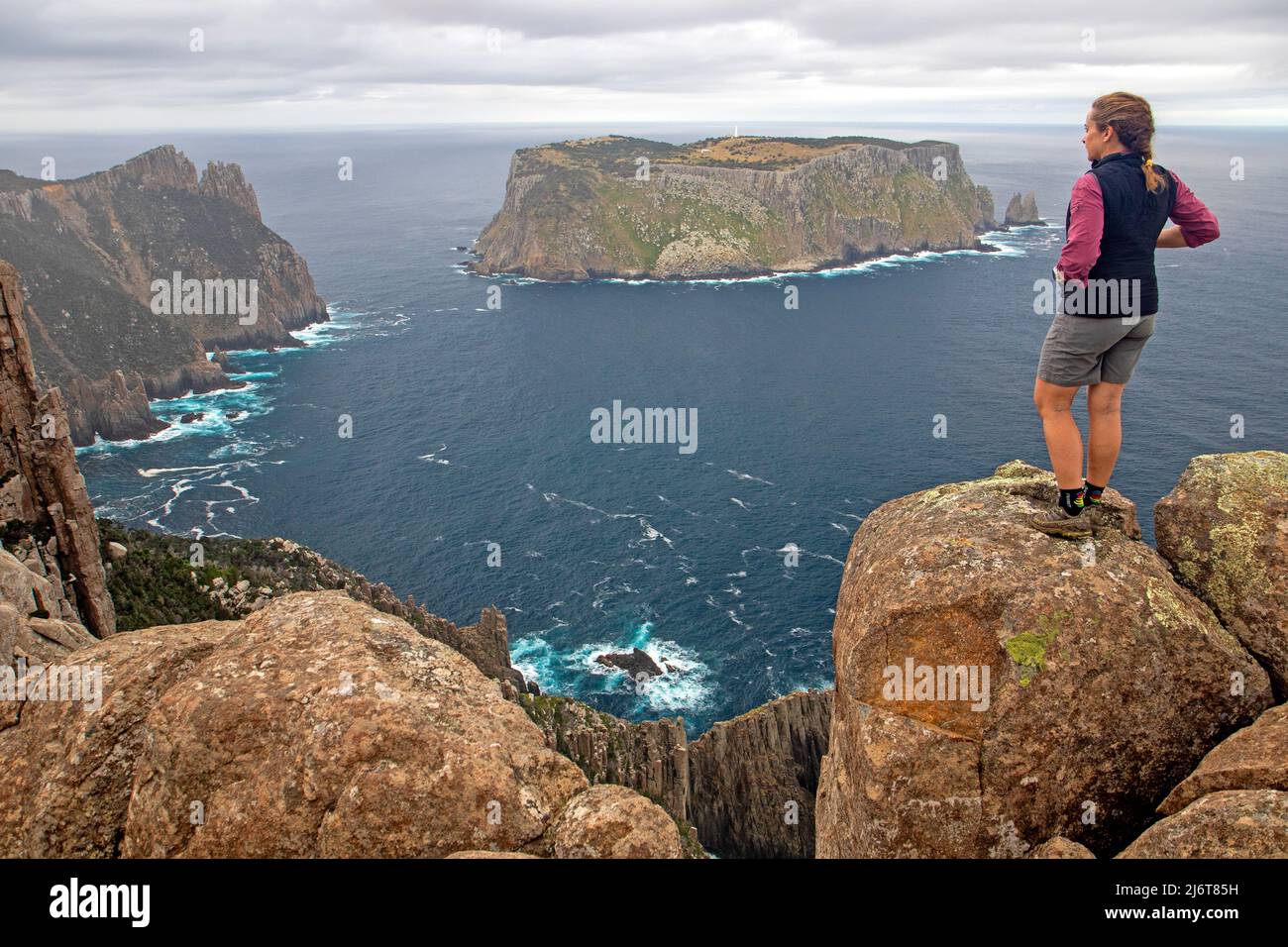 Woman atop the cliffs of Cape Pillar, looking out to Tasman Island ...