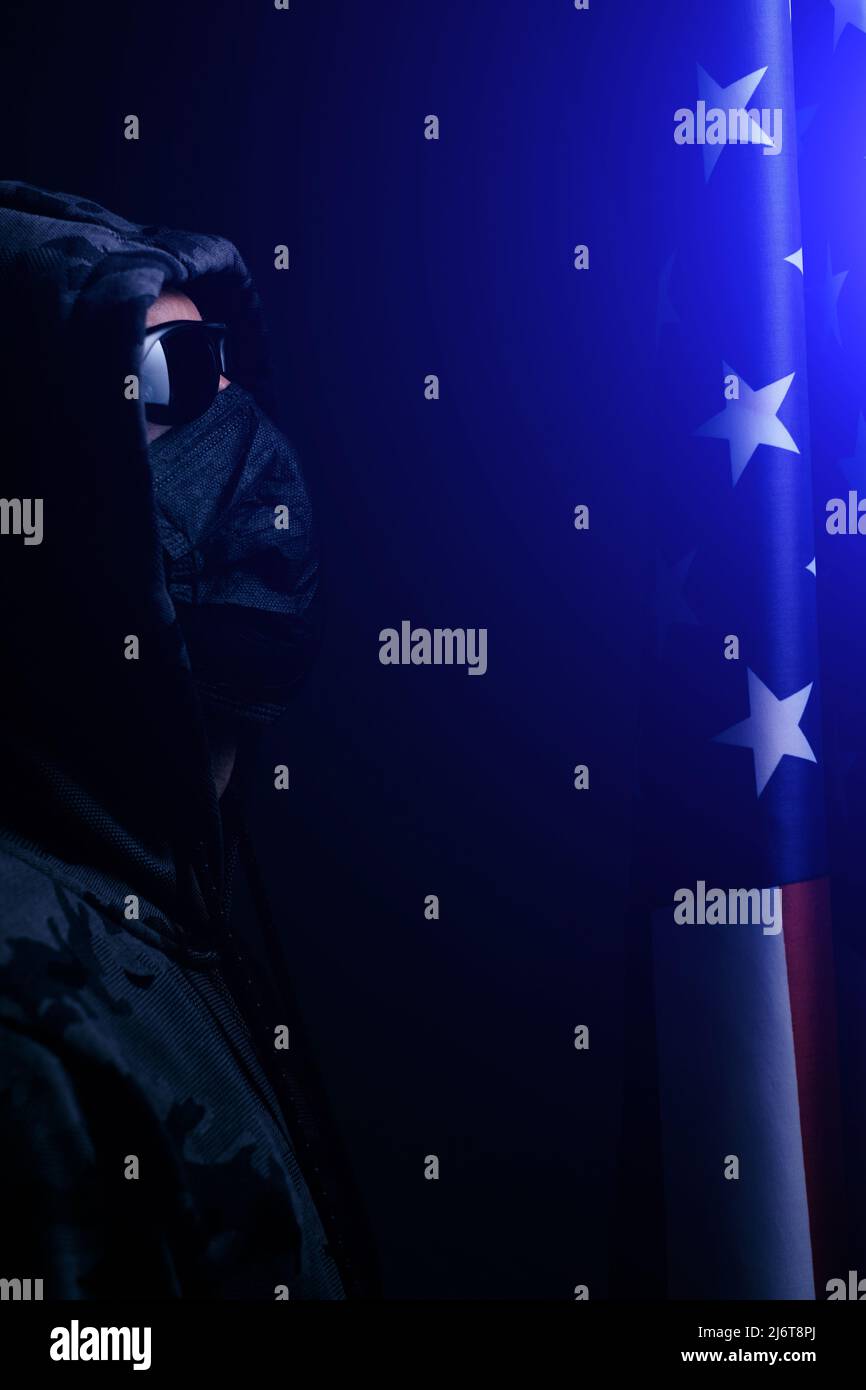 Hooded man wearing black glasses and mask looks flag of the United ...