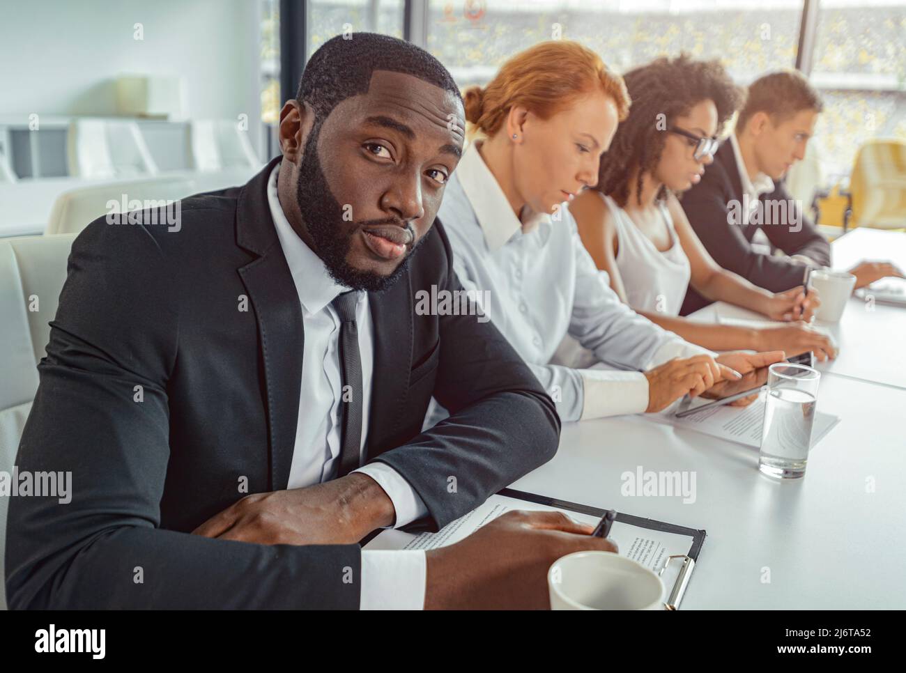 Portrait of African man in business suit sitting at table with co ...