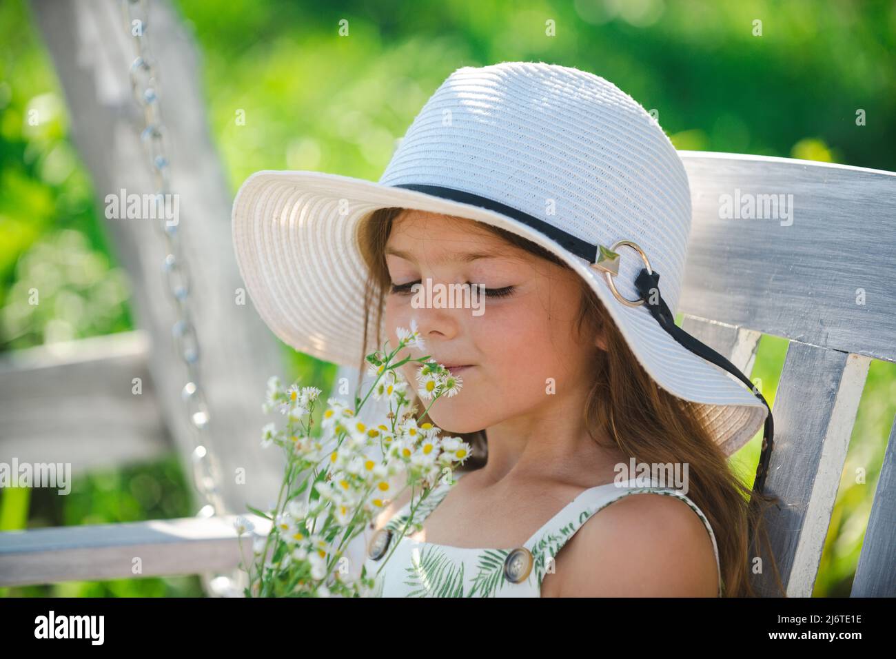Little child girl is smelling flowers on green backyard. Adorable kid ...