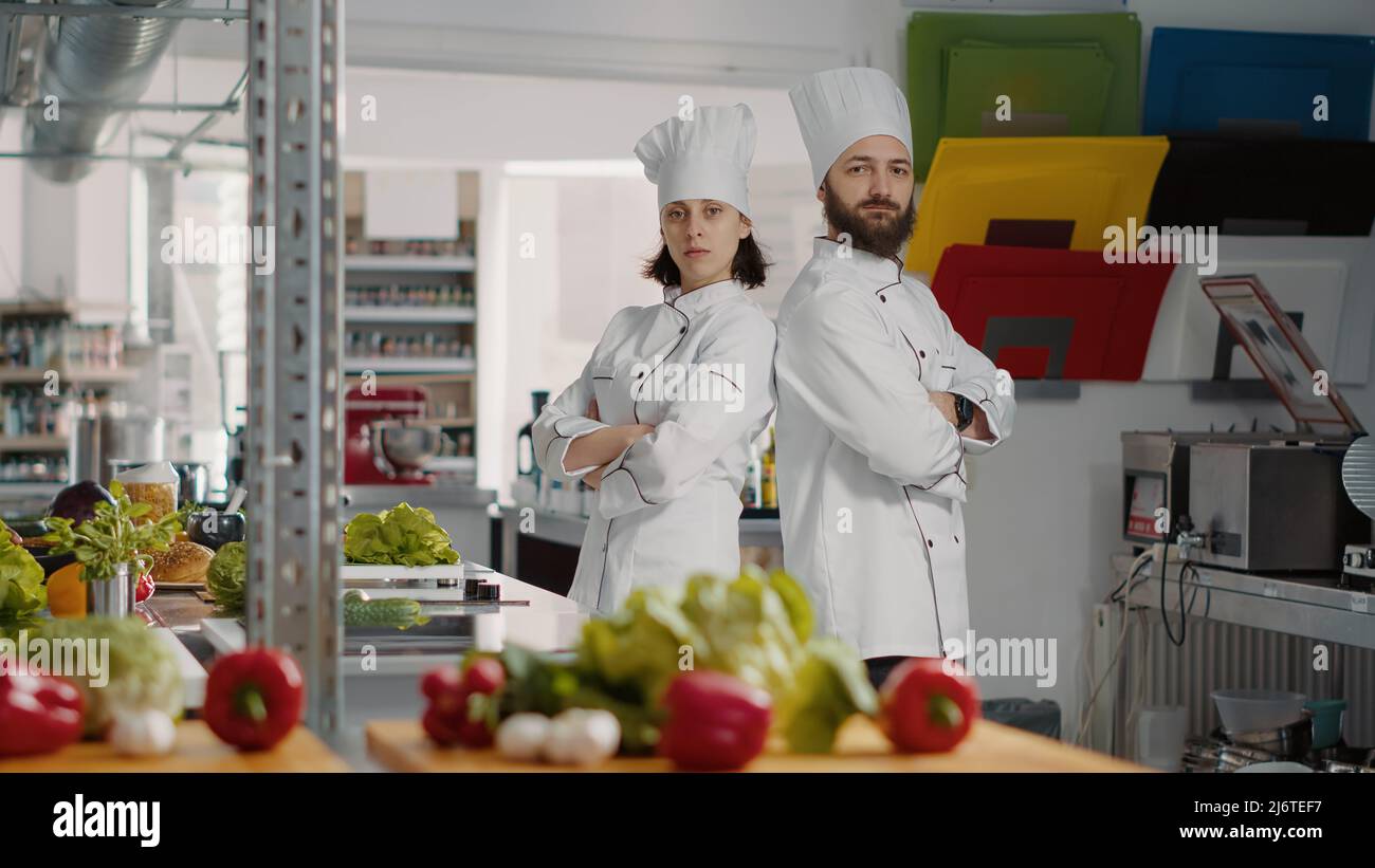 Portrait of authentic cooks sitting back to back in gourmet kitchen ...