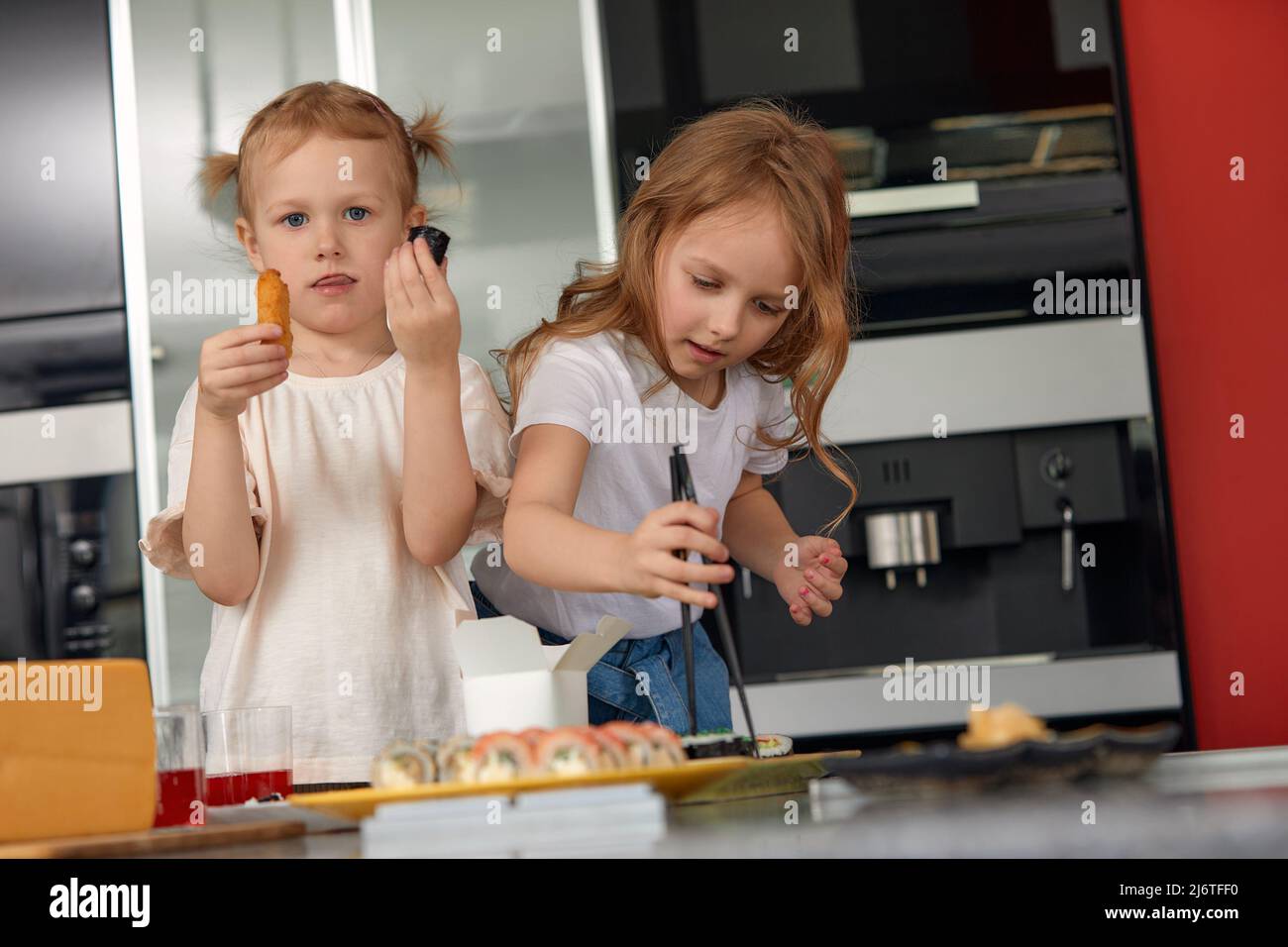 Two little girls siblings having fun and eating on the kitchen at home ...