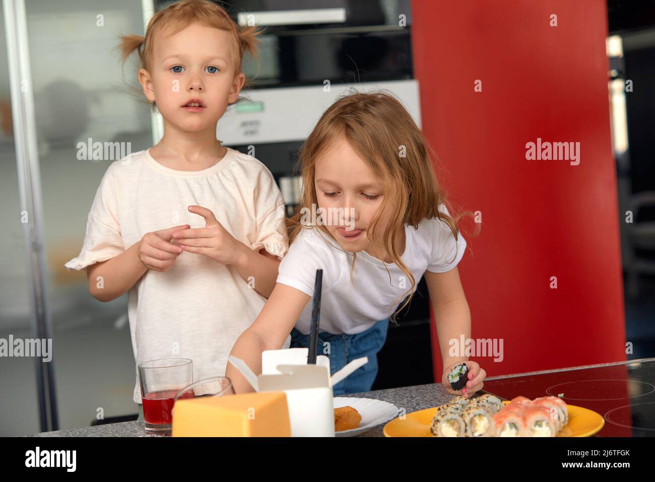 Two little girls siblings having fun and eating on the kitchen at home ...