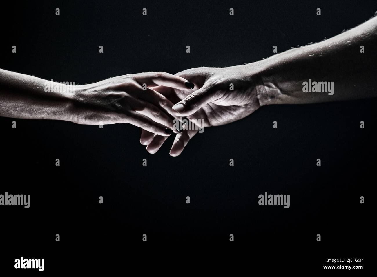 Two hands stretch each other, black background. Couple in love holding ...