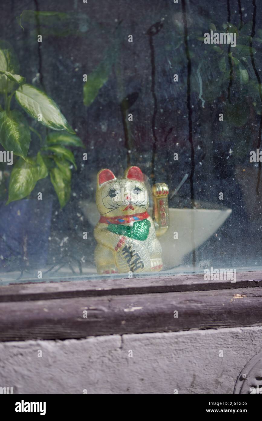 Japanese beckoning cat figurine, maneki-neko, behind dirty window pane ...
