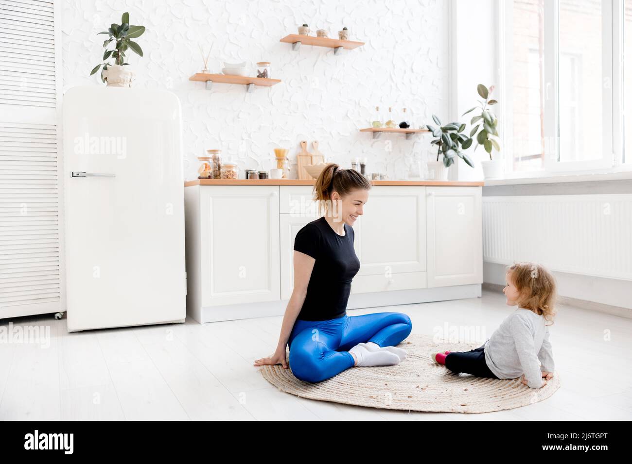 Mother and daughter are smiling confidently while doing yoga at home in ...