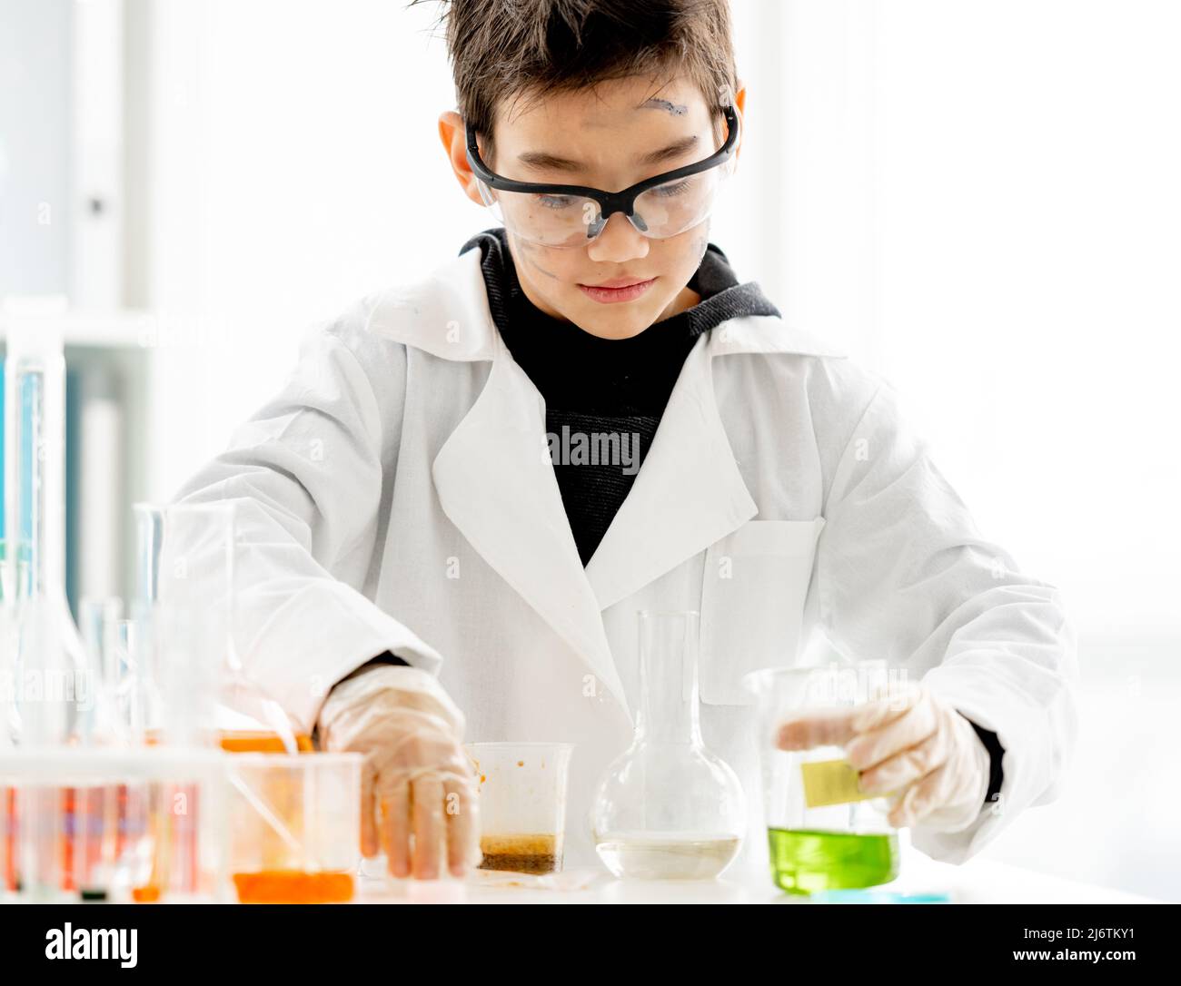 School boy wearing protection glasses with dirty face doing chemistry ...