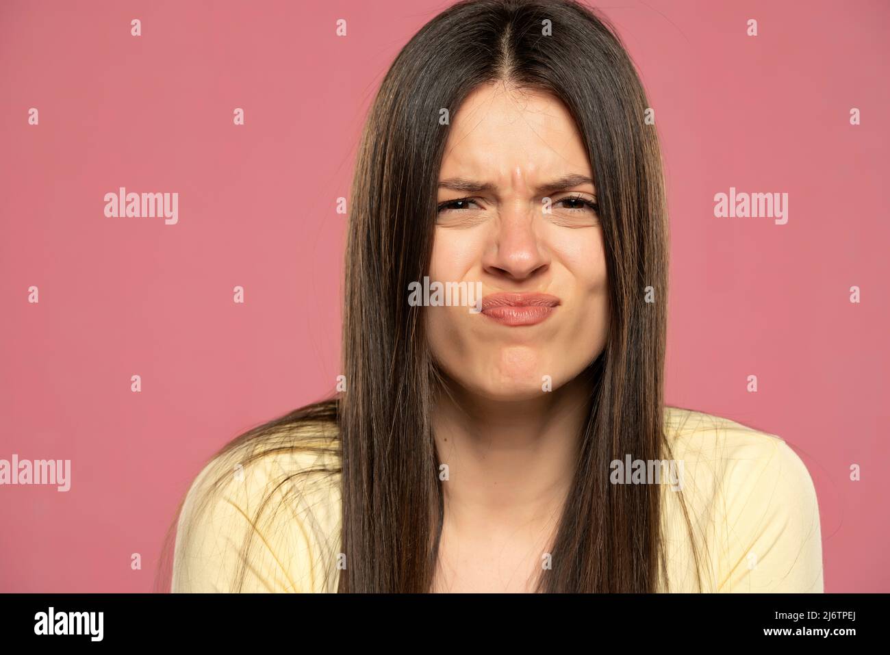Uncertain young brunette woman with sour face on a pink background ...