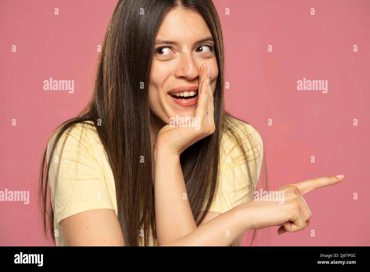 Woman telling secret and pointing on a pink background Stock Photo - Alamy