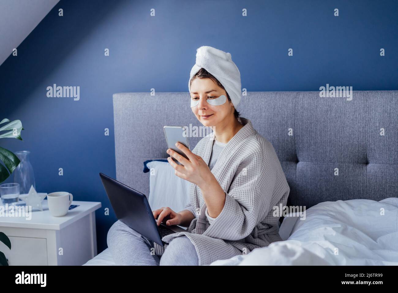 Woman in pajama and bathrobe with eyes patches and towel on her head ...