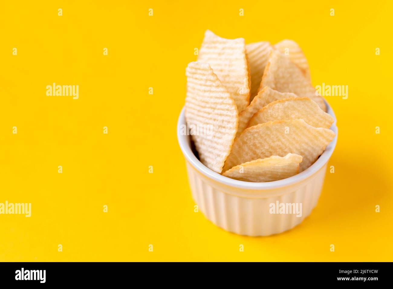 Riffled potato chips in white ceramic bowl on yellow background. Junk ...