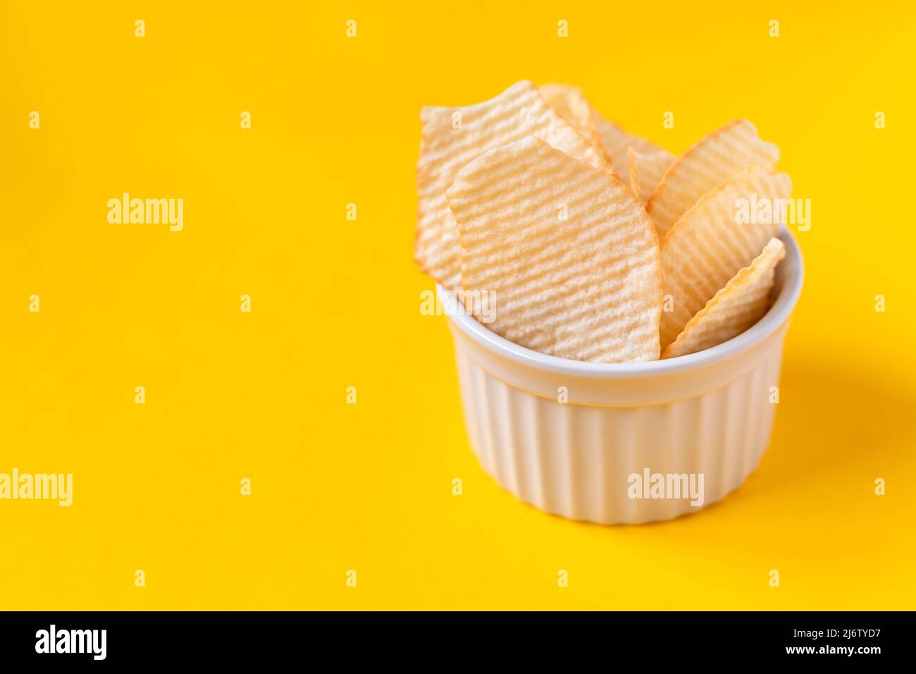 Riffled potato chips in white ceramic bowl on yellow background. Junk ...