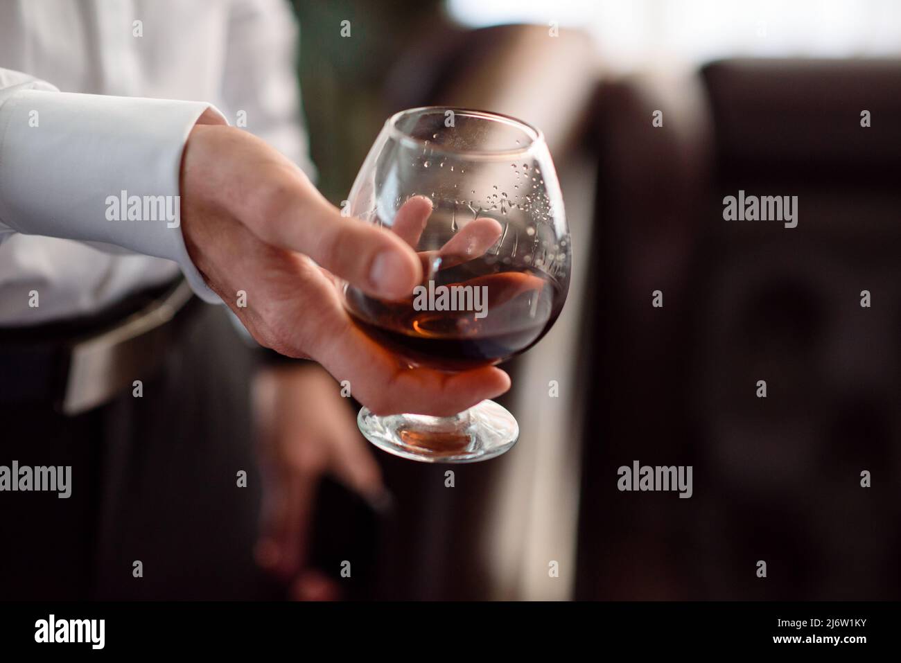 Hand holding a glass of cognac Stock Photo - Alamy