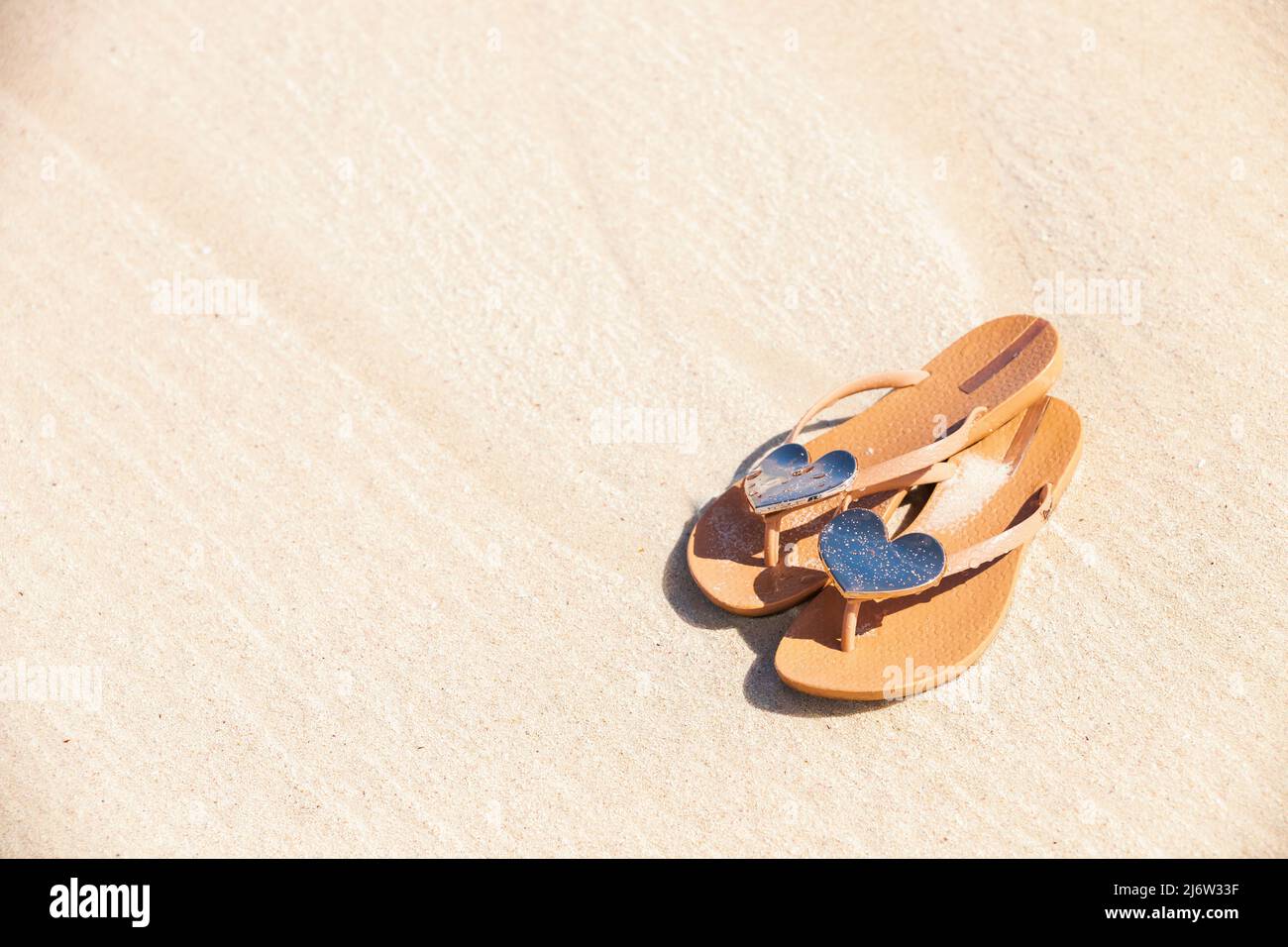 Beach flip-flops with a heart-shaped decoration stand on the wet sand ...