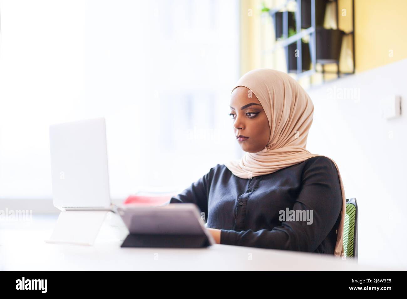 African american muslim girl with hijab working on a laptop in an ...